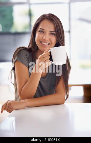 Relaxing with a cup of java. Shot of an attractive young woman drinking ...