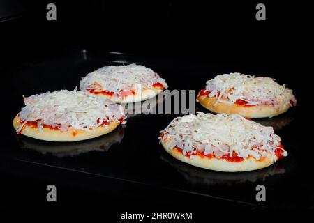 Four uncooked mini pizzas on tray in electric oven: front view, black background Stock Photo - Alamy