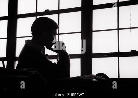 Silhouette of depressed and sad boy sitting and hugging his leg while ...