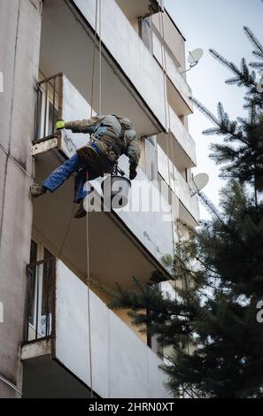 A worker is suspended by ropes, painting the exterior of a tall ...