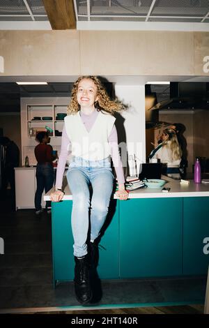 Happy biracial woman sitting at table in kitchen, using laptop and ...