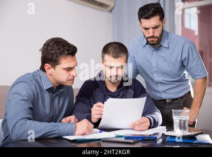 Three upset males with papers at table Stock Photo - Alamy