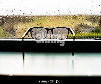 A pair of glasses resting on a window sill, observing the inclement ...