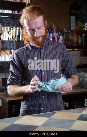 Optimistic male barkeeper with red hair pouring beer on tap into glass ...