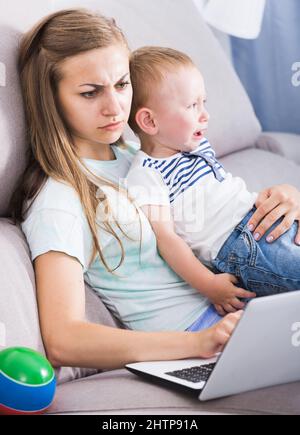 Perplexed female is having issue with work while child crying Stock ...