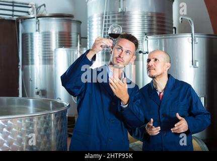 Two glad winery workers holding bottle of sparkling wine in aging ...