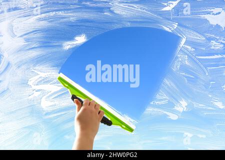 Female hand with squeegee and detergent washing glass against blue ...