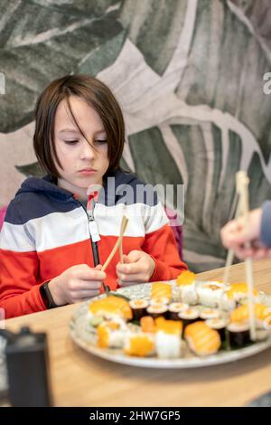 Child, eating japanese sushi and noodles with chopsticks in a ...