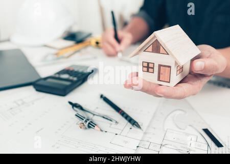 Architect engineer hands hold and show mini house model and use pen ...