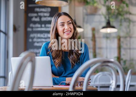 Smiling freelancer with laptop contemplating in cafe Stock Photo - Alamy