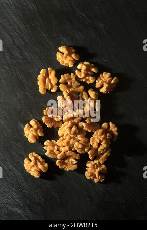 Close-up view of walnut kernels and whole walnuts scattered on a dark ...