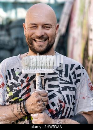 Portrait of smiling bald painter standing by workbench at workshop ...