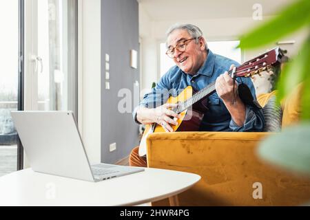 Man learning guitar through online tutorial on laptop sitting at table ...
