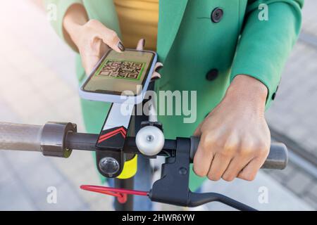 Commuter scanning QR code through smart phone on electric push scooter ...