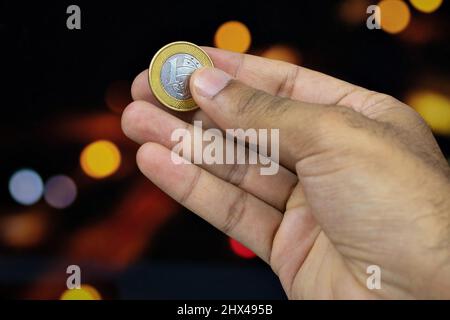 Holding a Brazilian money coin at a blurry lights background Stock ...