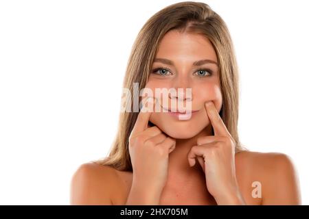 Portrait of young beautiful woman forcing her smile with her fingers on ...