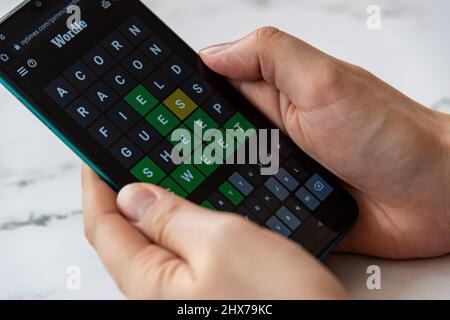 Hands playing Wordle game on phone on NYTimes.com website. Wordle is a ...
