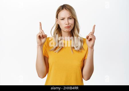 Suspicious young woman grimacing, pointing finger up, expressing doubt ...