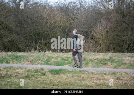 man with a laden backpack walking at speed along an unmade track road ...