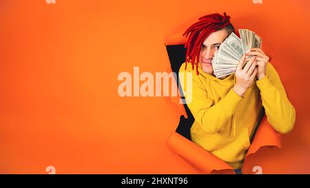 Young handsome man with money sticks out of hole of orange background ...