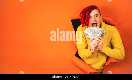 Young handsome man with money sticks out of hole of orange background ...