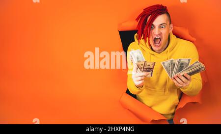 Young handsome man with money sticks out of hole of orange background ...