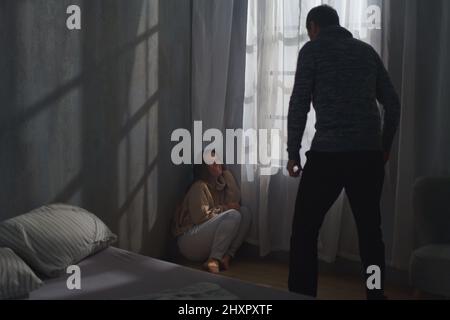 Scared woman sitting on ground and crying in fear of domestic violence ...