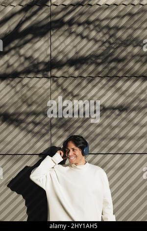 Cheerful male meloman in white shirt smiling looking at camera while ...