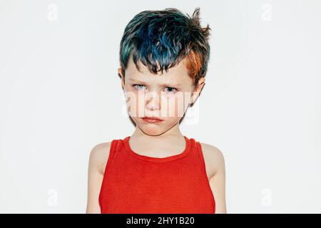 Rebellious boy with dyed hair looking away and touching face with hands ...