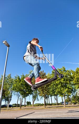 boy jumps with scooter at the skate park over a ramp and has fun Stock ...