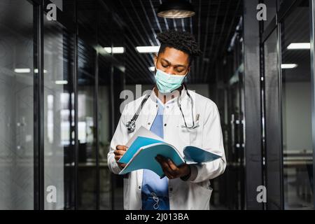 African doctor in mask with books in medical clinic. Black medical ...