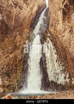 A high waterfall flows between steep rocks in a black and white nature ...