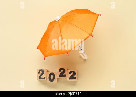 Open umbrella and wooden cubes with numbers 2022 on color background ...