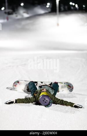 Snowboarder girl lying face down on slope. Night skiing in winter ...