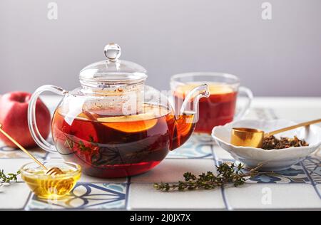 Fruit tea with apples and thyme in glass teapot and cup on table made ...
