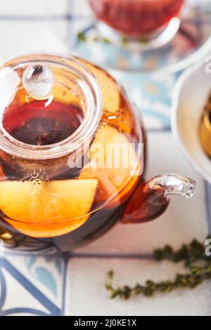 Fruit tea with apples and thyme in glass teapot and cup on the kitchen ...