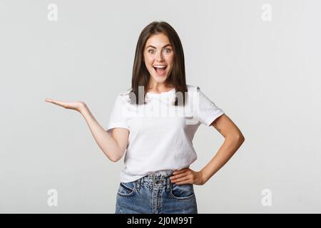 Excited beautiful girl extend arm, holding something on hand and ...