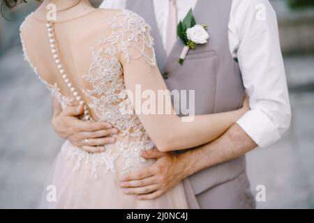 Hands of groom on the waist of bride in an embroidered lace dress ...