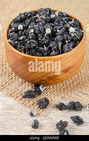 Black wolfberries or black goji berries, in a wooden bowl on table ...