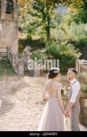 Bride and groom stand holding hands on the rocky shore. Waves hitting ...