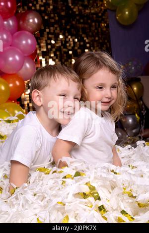 A boy and a girl play in a pile of cut white and gold paper Stock Photo ...