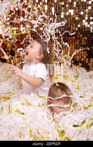 A boy and a girl play in a pile of cut white and gold paper Stock Photo ...