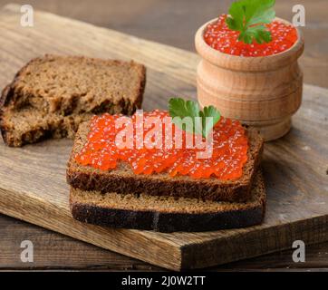 red salmon caviar lies on a piece of rye bread. Brown wooden table ...