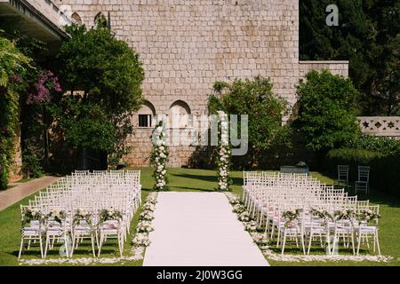 White carpet runs between rows of chairs decorated with flowers to the ...