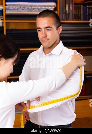 Experienced female tailor taking client body measurements Stock Photo ...