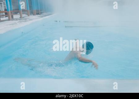 Fit swimmer male training swim in open winter swimming pool with fog ...