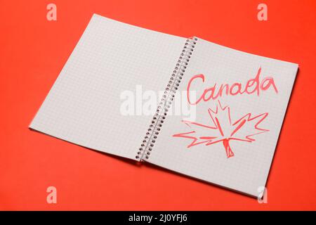 Open notebook with word CANADA, drawn maple leaf and paints on green ...