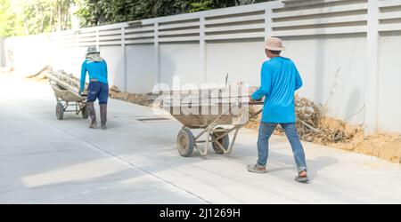 Two construction workers pulling a trolley carrying paving slabs in ...