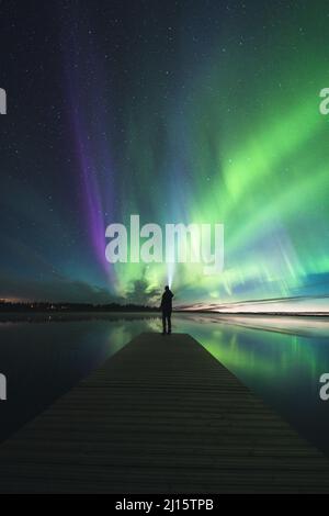 A vertical shot of a wooden dock under a beautiful Aurora Borealis ...