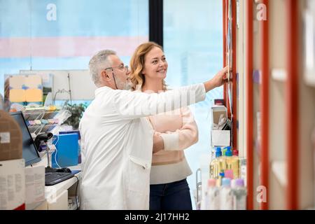 Smiling pharmacist helping customer with medicine in pharmacy store ...